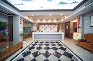 Área de recepção de hotel com balcão de check-in, piso xadrez preto e branco e teto com claraboia.