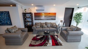 Uma sala de estar moderna com dois sofás cinzentos, uma mesa de centro e uma grande pintura de um pôr do sol.