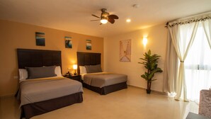 Quarto de hotel com duas camas, um ventilador de teto, luminárias fixadas na parede, um vaso de planta e vista para o exterior através de cortinas.