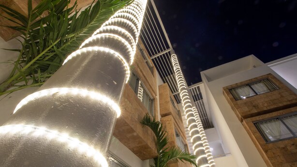 Um edifício com design arquitetônico moderno, apresentando uma série de colunas cilíndricas iluminadas e uma varanda com guarda-corpo de metal.