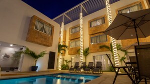 Piscina com espreguiçadeiras e guarda-sóis, cercada por um edifício com vários andares e janelas.