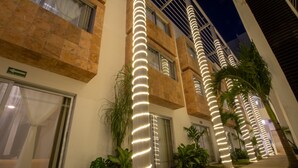 Hotel com design moderno, apresentando uma série de colunas iluminadas e um jardim bem cuidado com diversas plantas.