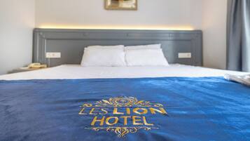 Uma cama com um cobertor azul e o logotipo do Les Lion Hotel, uma cabeceira cinza e um quadro na parede.