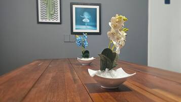 Uma mesa de madeira com três tigelas de cerâmica branca contendo flores brancas, em frente a uma parede cinza com quadros.