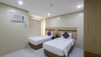 Quarto de hotel com duas camas, um ventilador de teto e ar-condicionado fixado na parede.