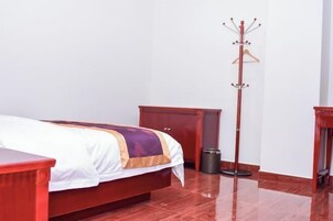 Quarto de hotel bem arrumado, com uma cama, mesa de cabeceira de madeira, cabideiro e lixeira.