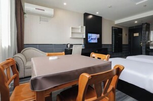 Quarto de hotel com mesa de jantar, cadeiras, sofá, televisão e cama.