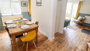 Uma área de refeições com uma mesa de madeira posta para quatro pessoas, cadeiras amarelas e vista para a sala de estar adjacente.