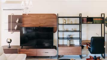 Uma sala de estar moderna com uma TV de tela plana, estantes de madeira com objetos decorativos, uma cadeira de escritório preta e um globo em uma mesinha lateral.