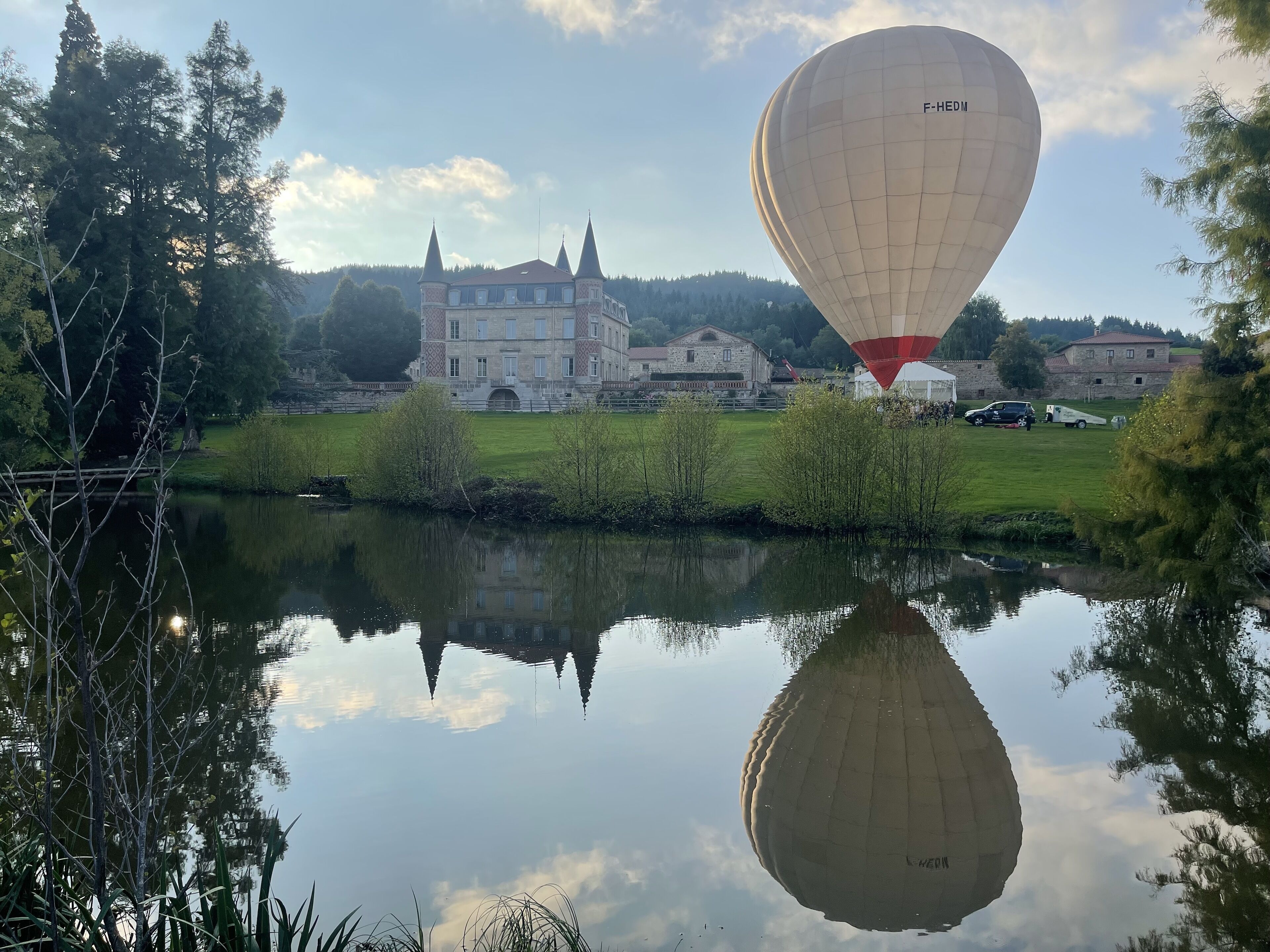 Um balão de ar quente sobre um corpo d'água, com um edifício semelhante a um castelo ao fundo.