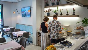 Espaço de café da manhã com mesas, cadeiras e um buffet de frutas e pães.