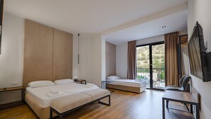 Quarto de hotel moderno com uma cama grande, um sofá, uma mesinha e uma varanda com cortinas.