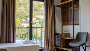 Quarto de hotel com cama, escrivaninha, cadeira e varanda com cortinas.