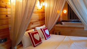 Quarto de cabana de madeira com uma cama, dois travesseiros em formato de coração e uma banheira.