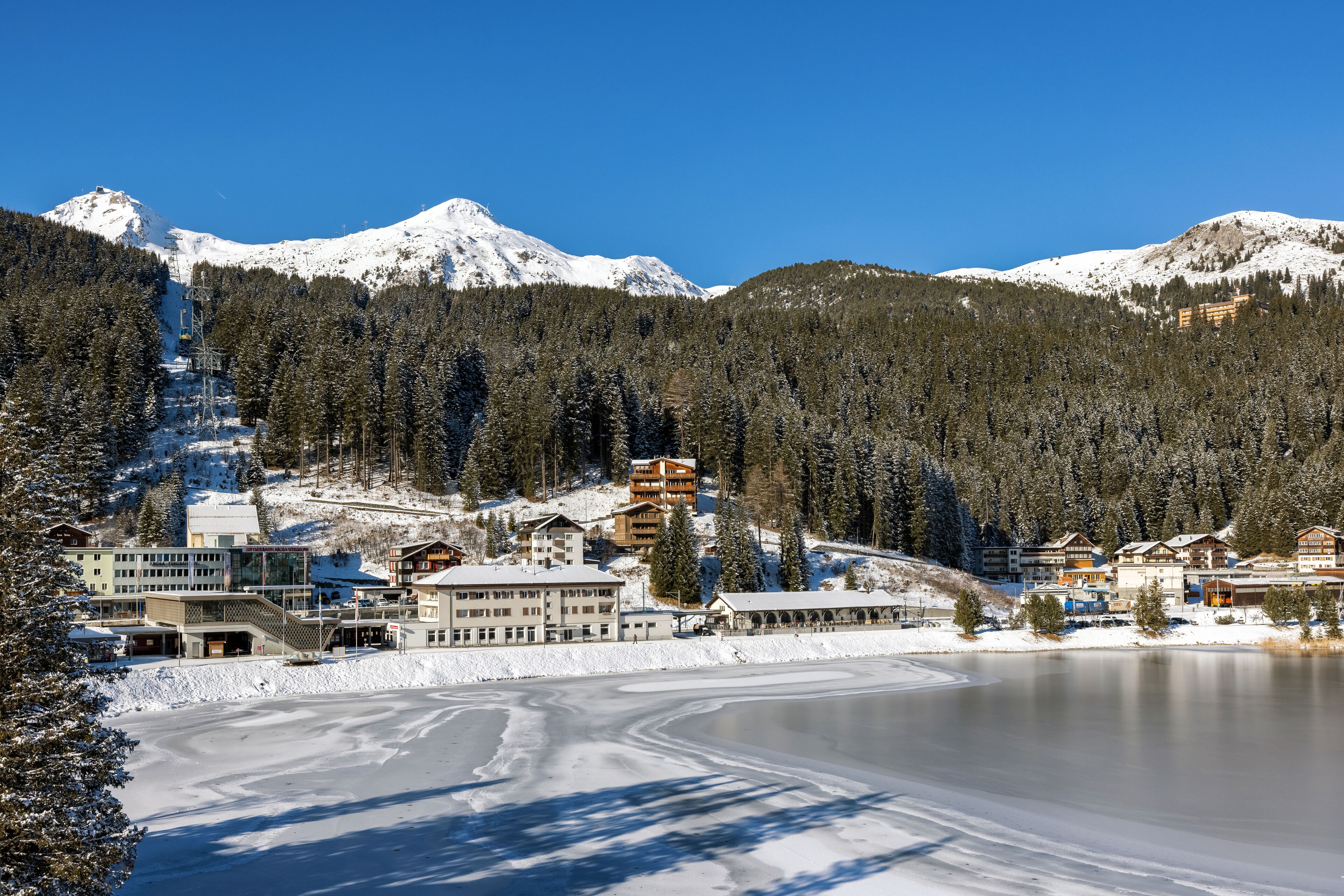Montanha coberta de neve com uma estação de esqui, incluindo edifícios e um lago congelado.