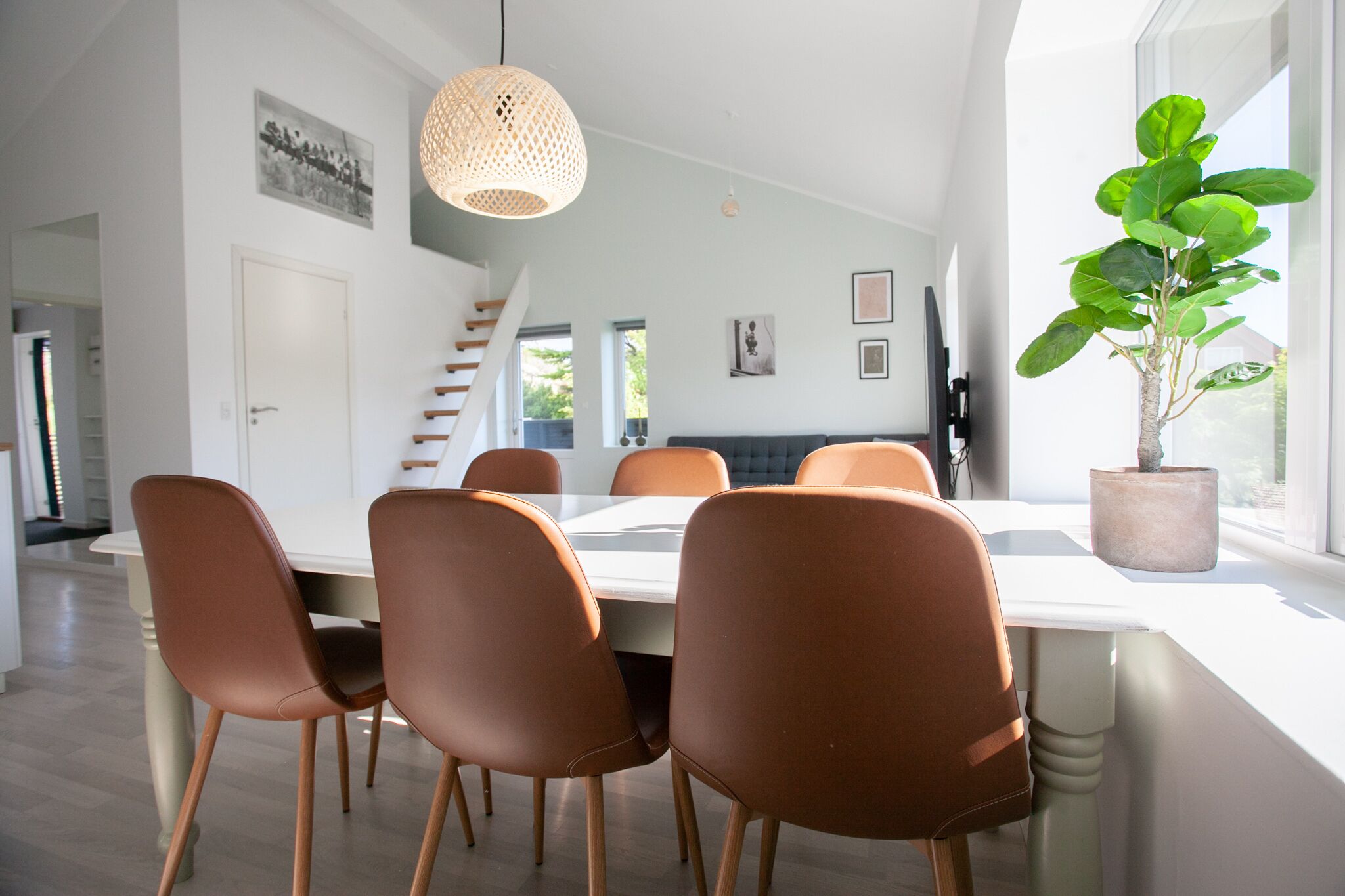 Uma sala de jantar moderna com uma mesa branca, cadeiras marrons e um vaso de planta.