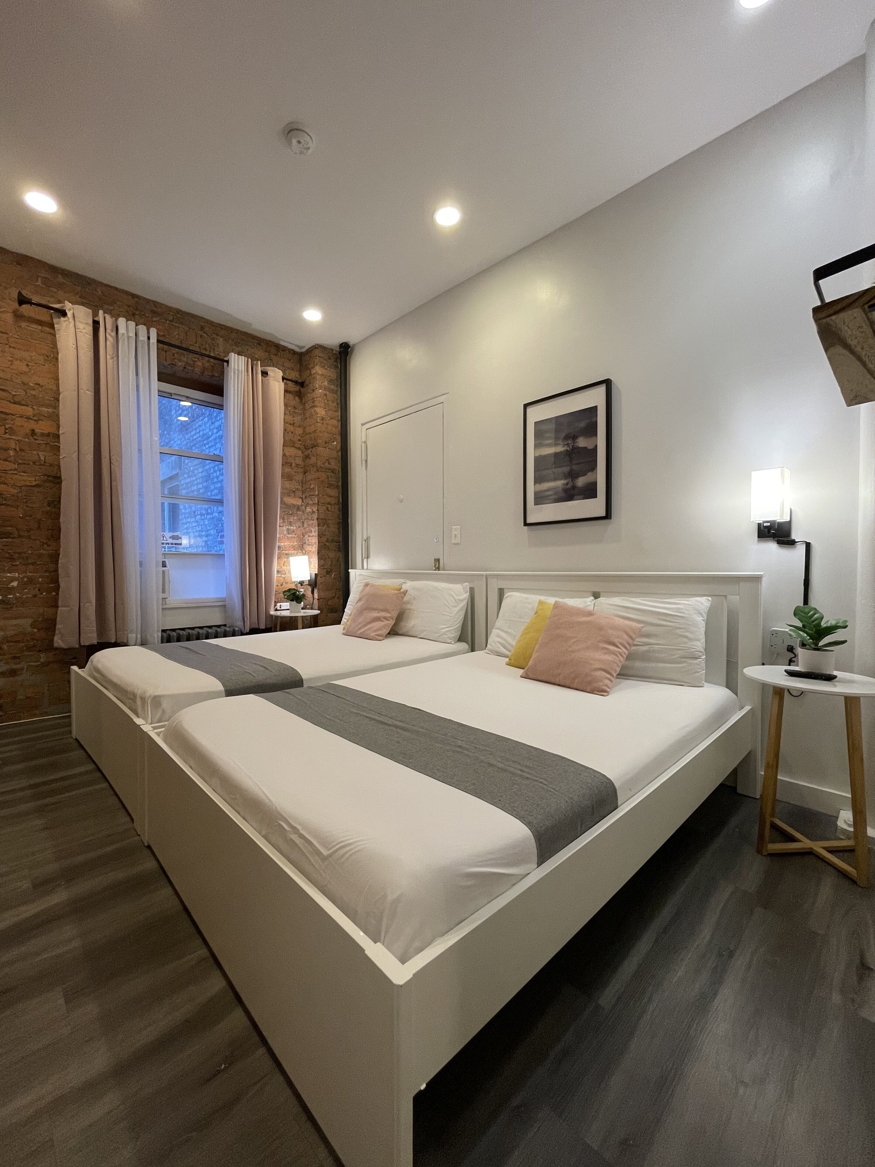 Quarto de hotel moderno com uma cama grande, parede de tijolos e janela com cortinas.
