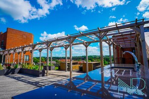 Um terraço no telhado com pérgola, mobiliário de exterior e uma cozinha moderna.