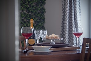 Uma mesa com uma garrafa de prosecco, dois copos de vinho tinto, um prato de sobremesa e uma tigela de chantilly.
