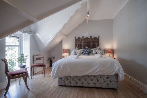 Quarto com uma cama grande, cabeceira de madeira, duas luminárias de cabeceira e uma janela com vista para o verde.