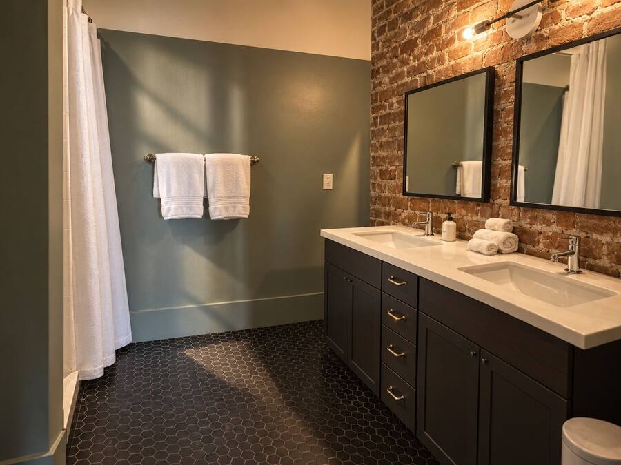 Um banheiro moderno com duas pias, armários escuros e uma parede decorada com tijolos.