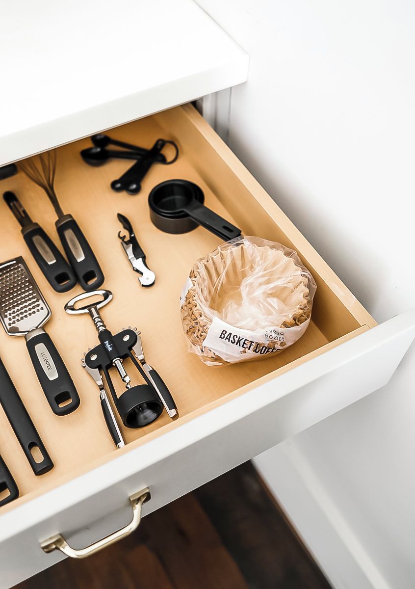 Uma gaveta com diversos utensílios de cozinha e uma cesta com mantimentos.