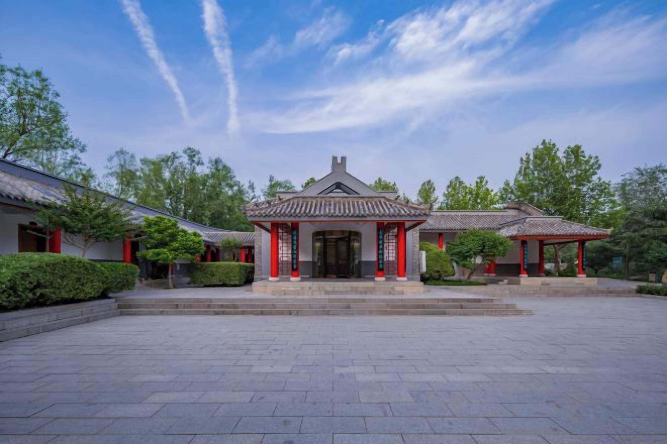 Um pavilhão tradicional chinês com telhado ladrilhado, rodeado por um pátio com piso de pedra.