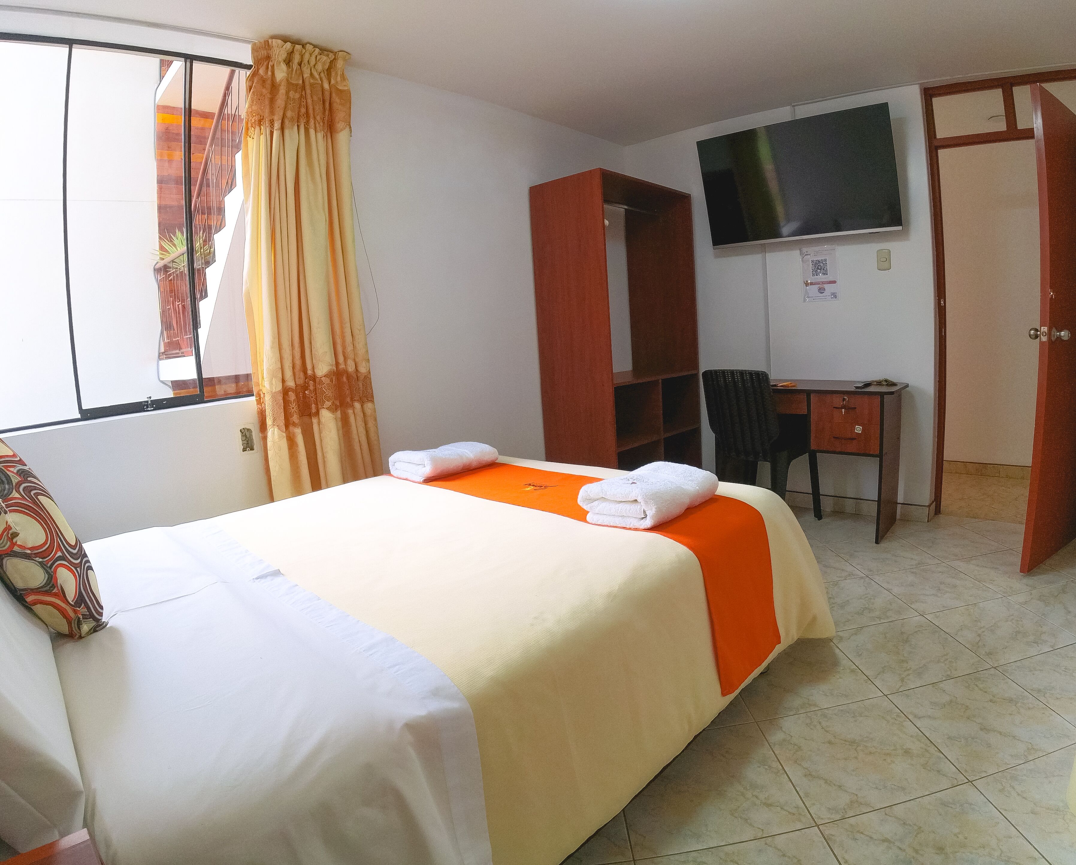 Quarto de hotel com cama, escrivaninha, televisão e guarda-roupa.
