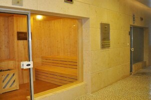 Uma sauna com banco de madeira e porta de vidro, anexa a uma parede com uma placa e uma porta.