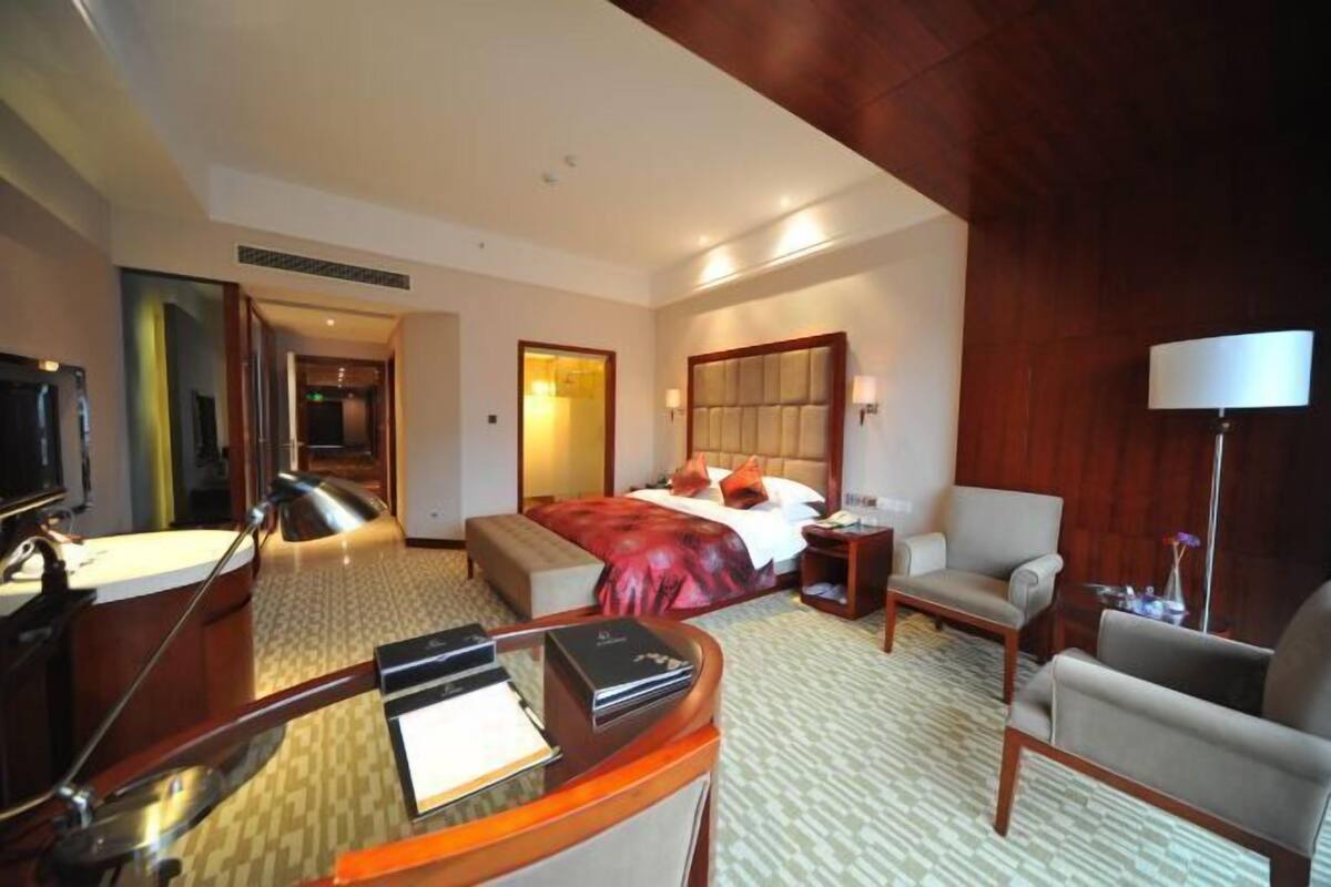 Quarto de hotel com uma cama, escrivaninha com abajur, cadeira e mesa de cabeceira.