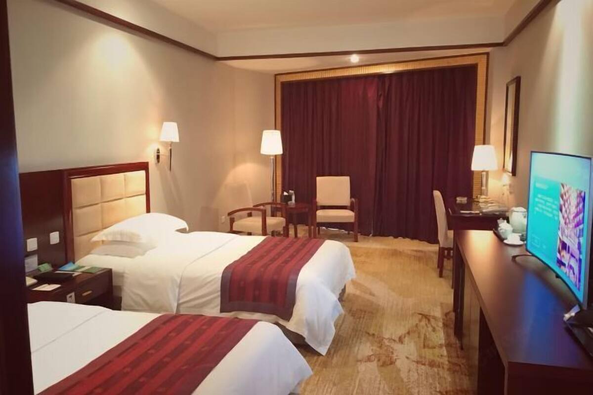 Quarto de hotel com duas camas, uma escrivaninha, uma cadeira e uma televisão.
