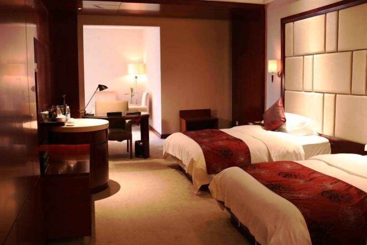 Quarto de hotel com duas camas, uma escrivaninha, uma cadeira e um abajur.