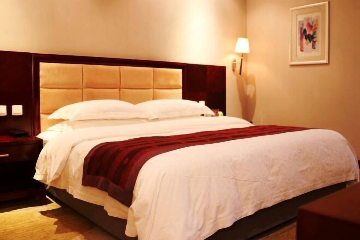 Quarto de hotel com uma cama grande, uma mesa de cabeceira, um abajur e um quadro na parede.