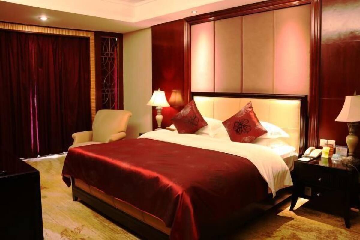 Quarto de hotel com uma cama grande, uma cadeira, uma mesa de cabeceira e uma cortina.