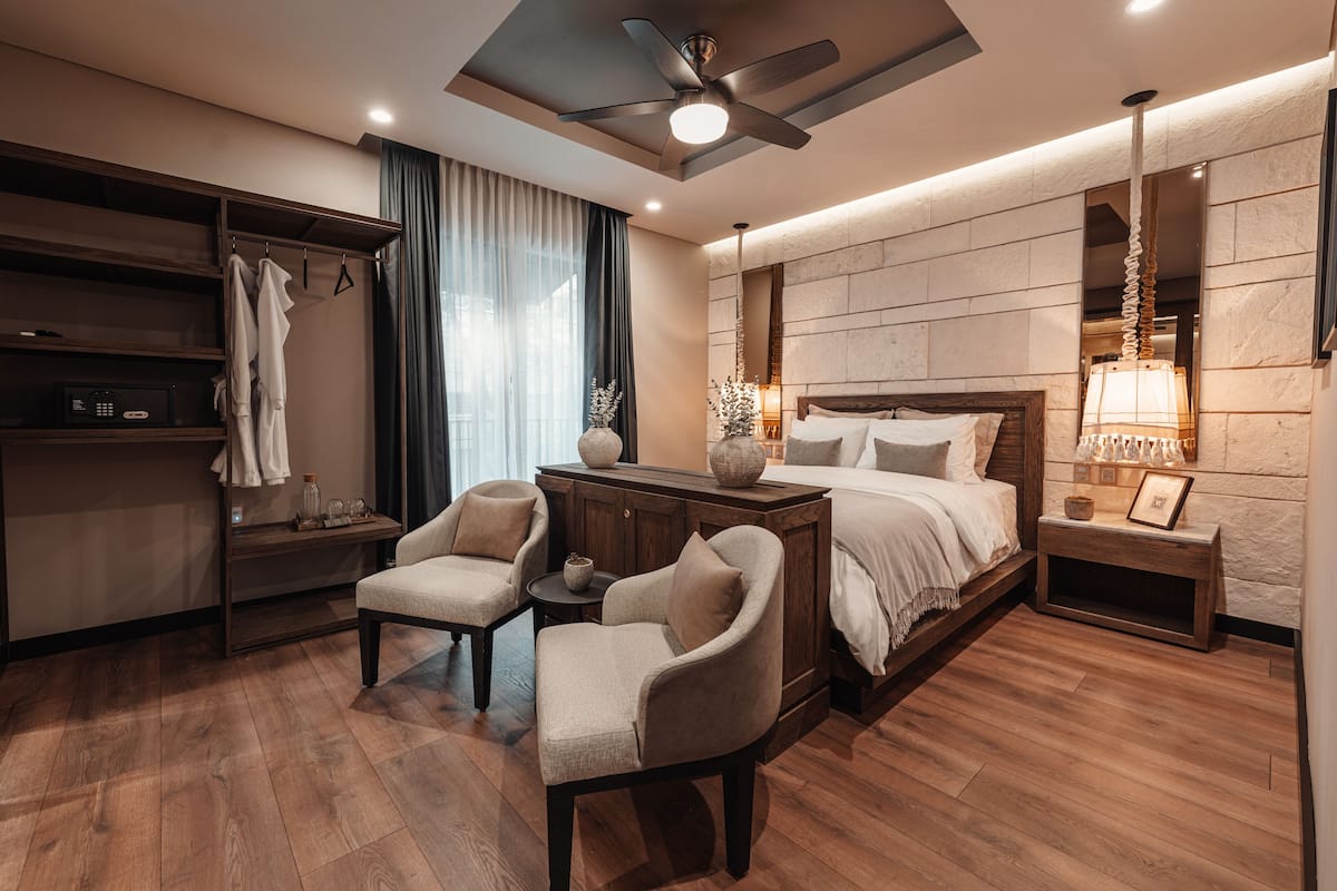 Quarto de hotel moderno com uma cama, duas poltronas, uma mesa pequena, um guarda-roupa e um ventilador de teto.