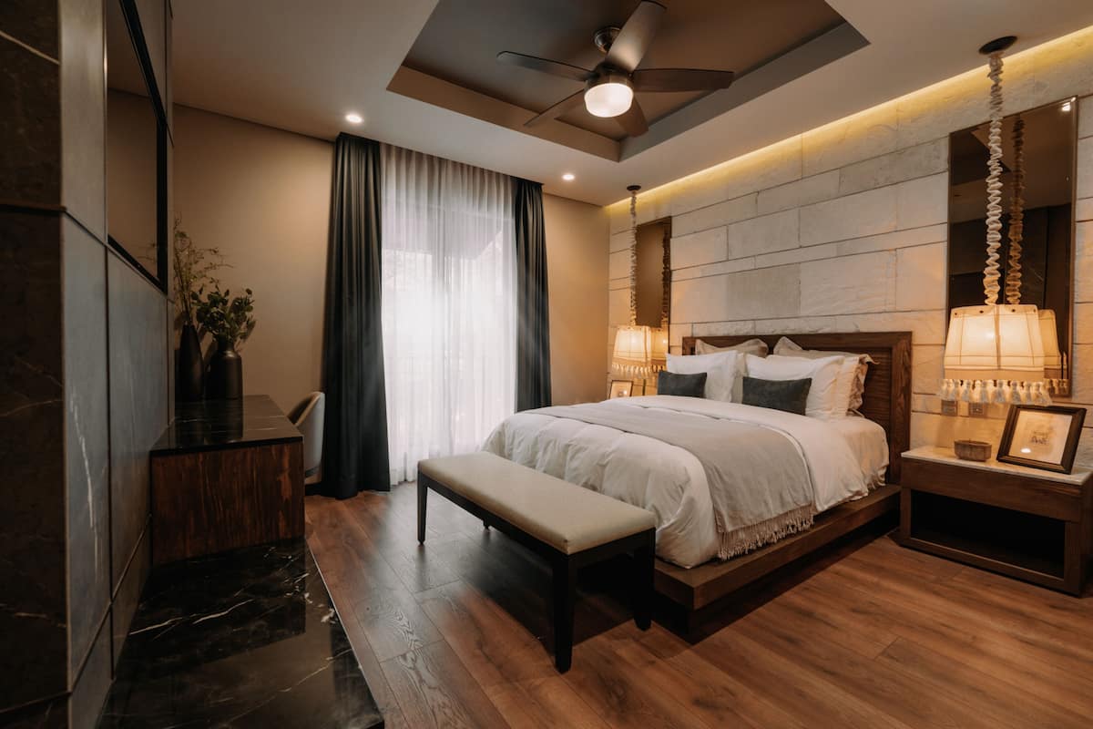 Um quarto moderno com uma cama grande, luminárias de cabeceira, um banquinho e um ventilador de teto.