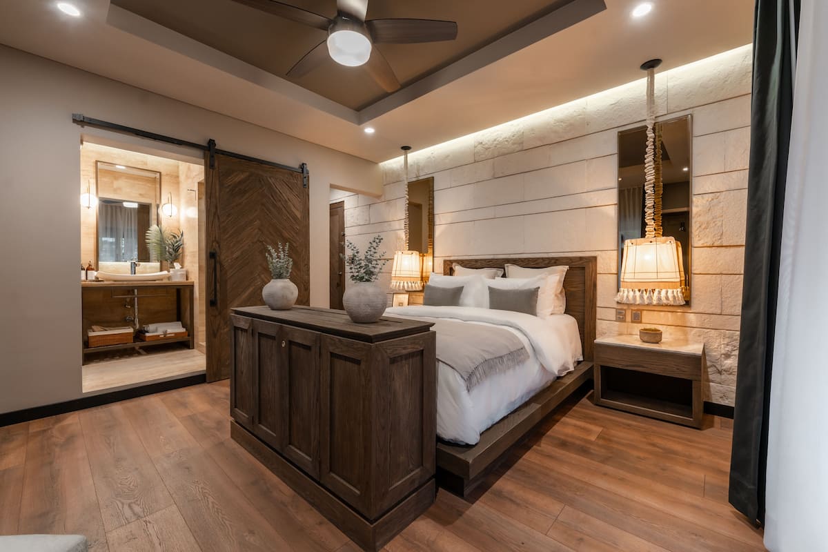 Quarto moderno com cama de madeira, mesas de cabeceira, um espelho grande e um ventilador de teto.