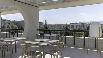 Terraço no telhado com mesas e cadeiras, proporcionando vista dos edifícios ao redor.