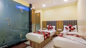 Quarto de hotel com duas camas, box de vidro para o chuveiro e ventoinha no teto.