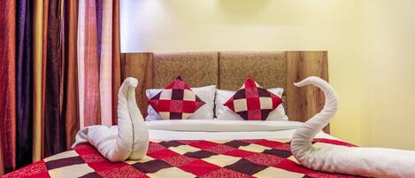 Uma cama bem arrumada com um cobertor quadriculado vermelho e bege, dois cisnes brancos sobre a cama e uma cabeceira de madeira.