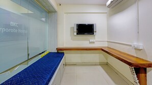 Um quarto pequeno com uma cama, uma televisão presa na parede e um aparelho de ar condicionado.
