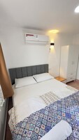 Quarto com cama, guarda-roupa, ar condicionado e luminária na parede.