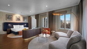 Quarto de hotel moderno com uma cama grande, uma escrivaninha, um sofá e vista para um edifício pela janela.