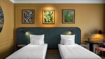 Quarto de hotel com duas camas de solteiro, uma cabeceira grande e três obras de arte emolduradas na parede.