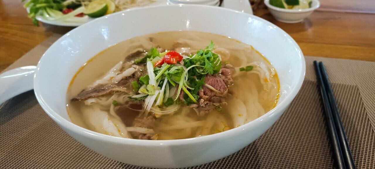Uma tigela de sopa com macarrão e carne, decorada com ervas e pimenta.