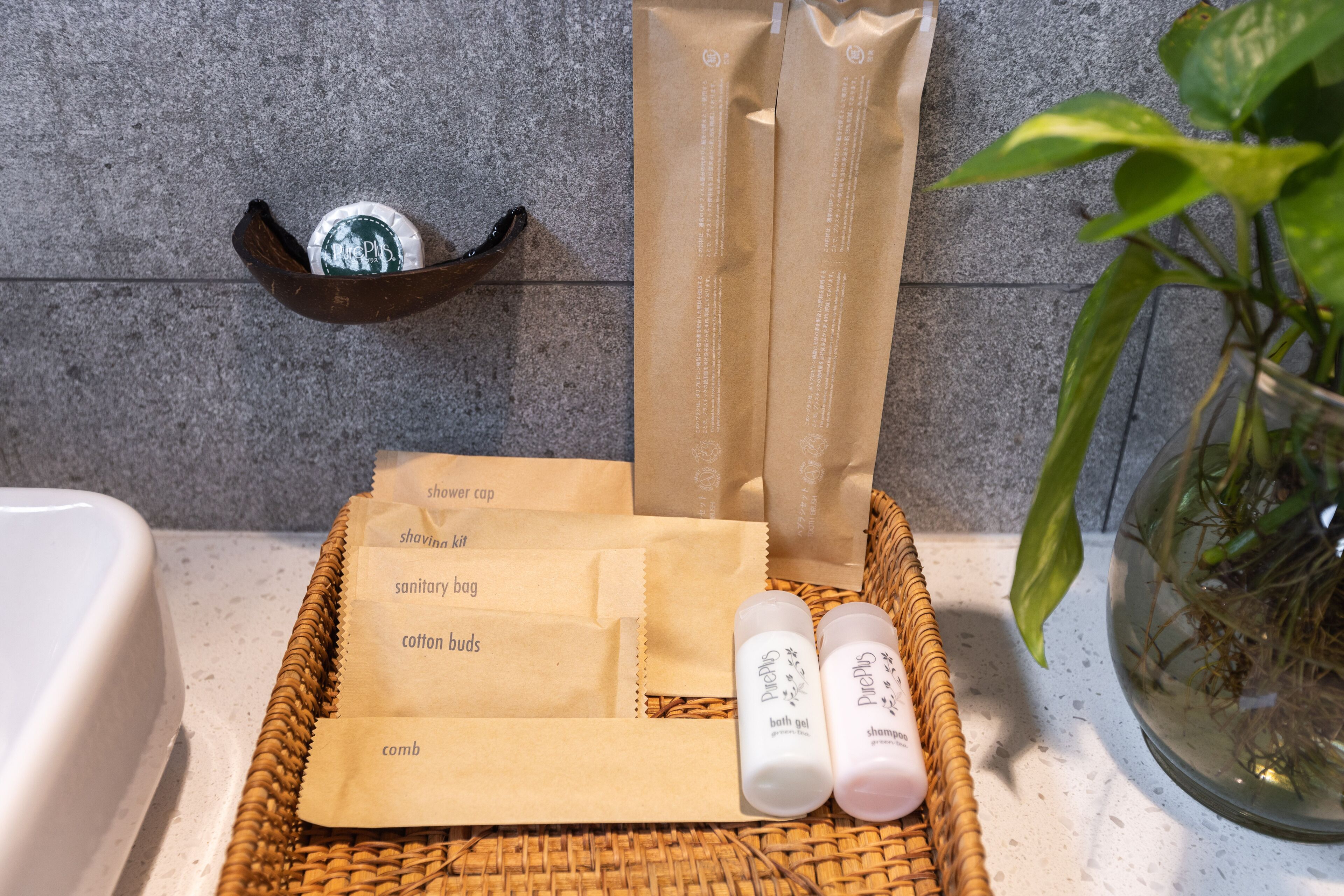 Casa de banho com cesto de vime contendo produtos de higiene, touca de duche, saco de higiene, cotonetes, pente e garrafas de gel de banho.