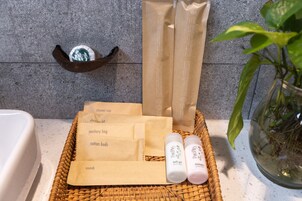 Casa de banho com cesto de vime contendo produtos de higiene, touca de duche, saco de higiene, cotonetes, pente e garrafas de gel de banho.
