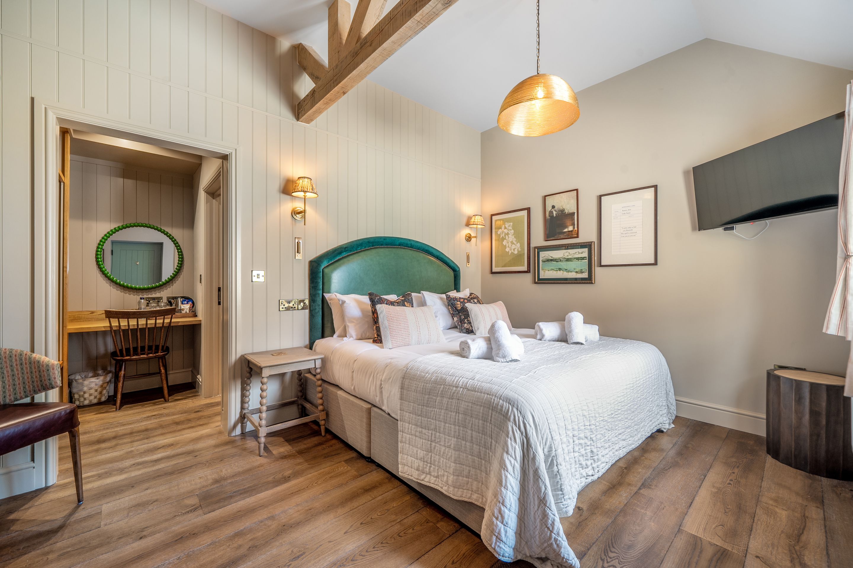 Quarto com cama, mesa de cabeceira, luminária, obra de arte na parede e televisão.