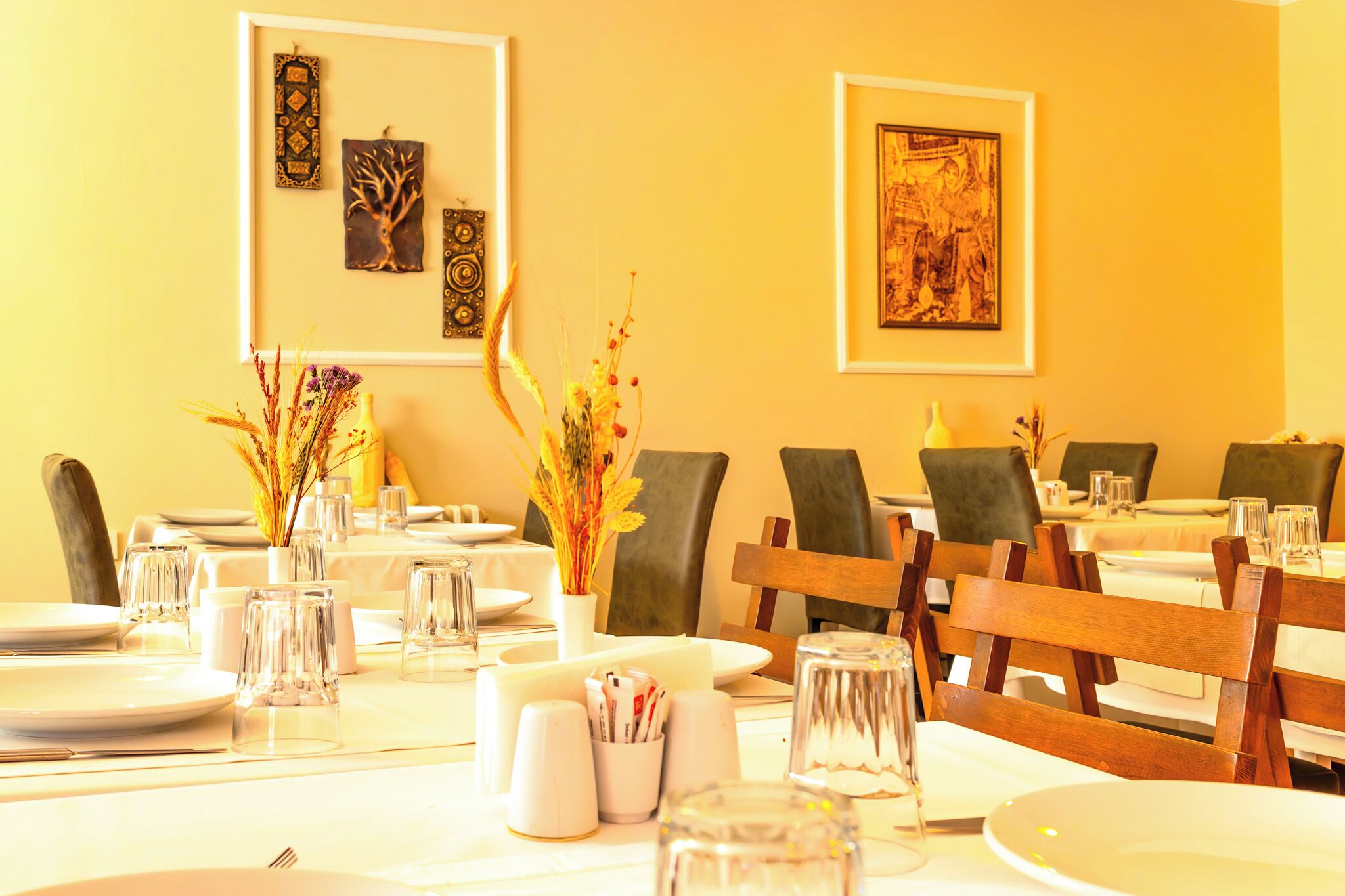 Uma sala de jantar com mesas postas, cadeiras e objetos decorativos.