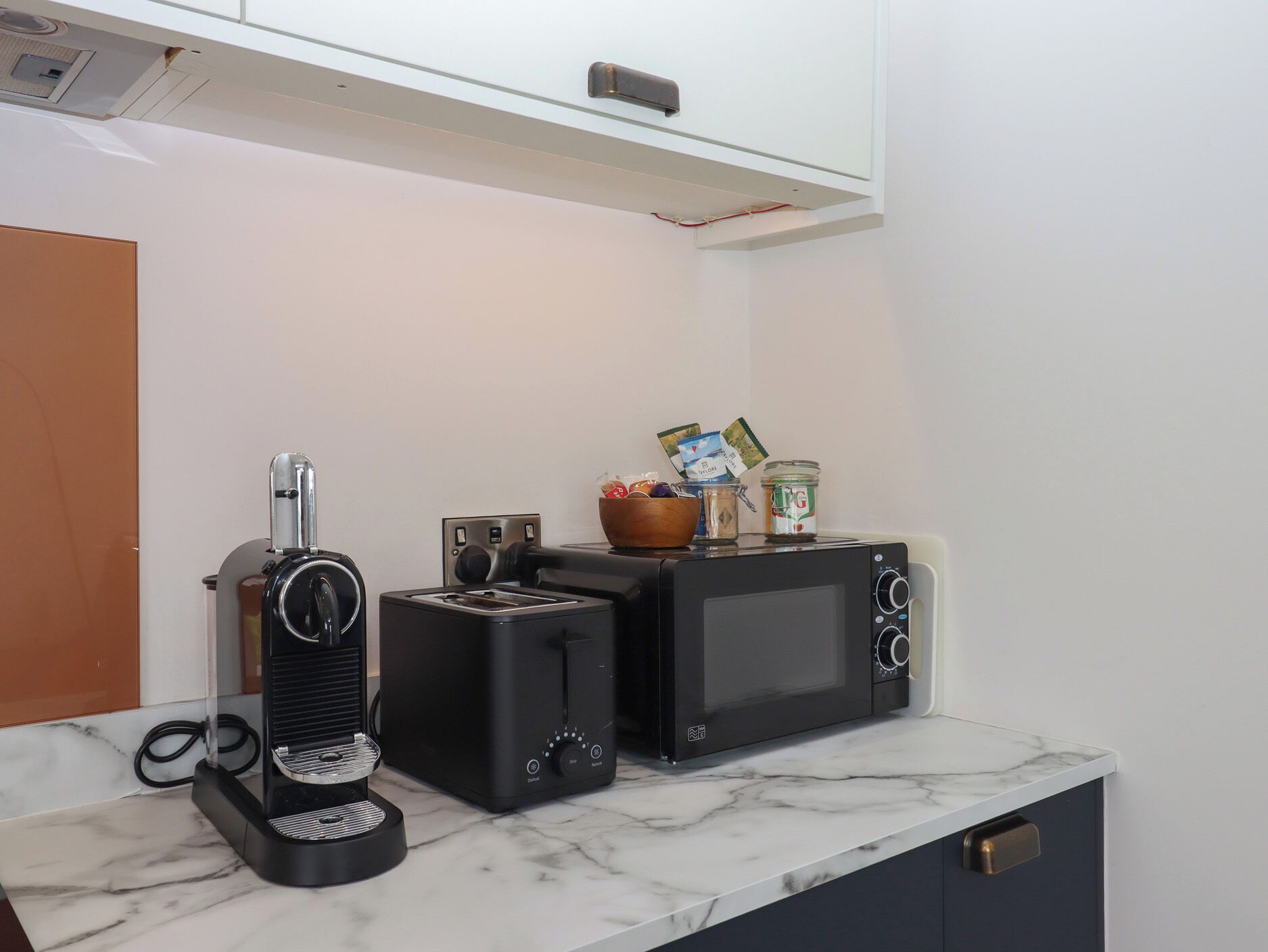 Cozinha com cafeteira, torradeira e micro-ondas em bancada de mármore.